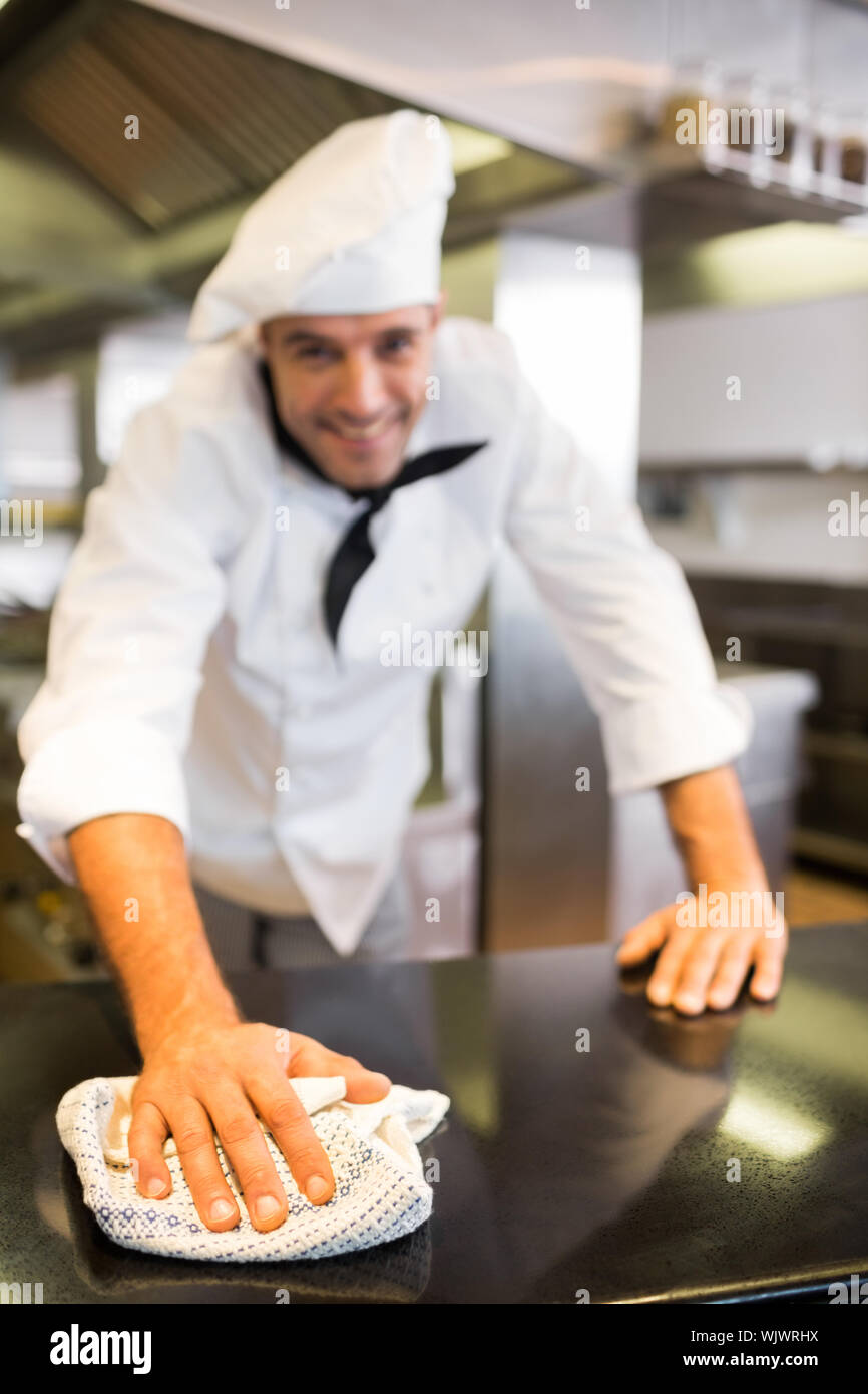 Portrait of a smiling male cook wiping the counter top in the kitchen ...