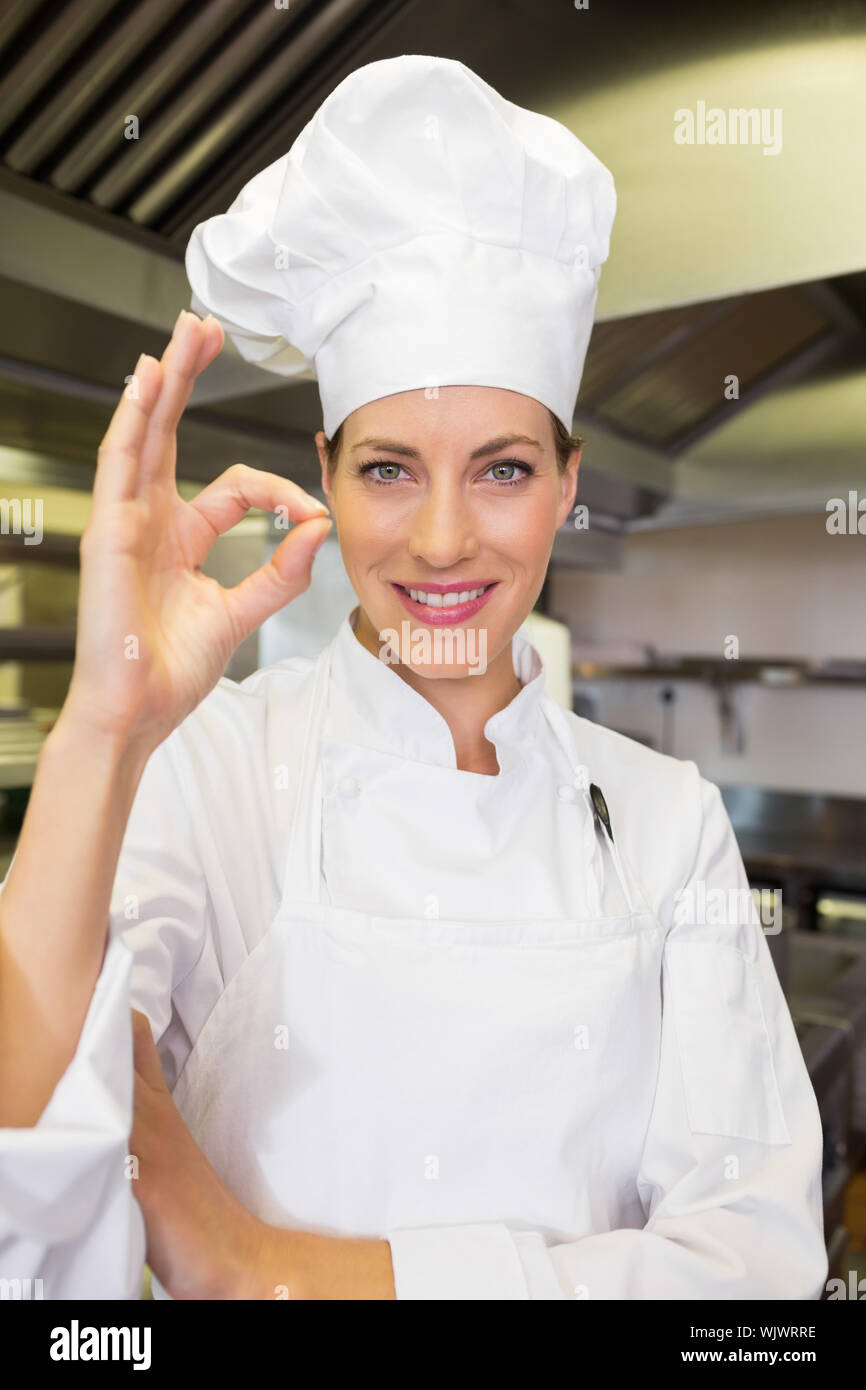 Portrait of a smiling female cook gesturing okay sign in the kitchen ...