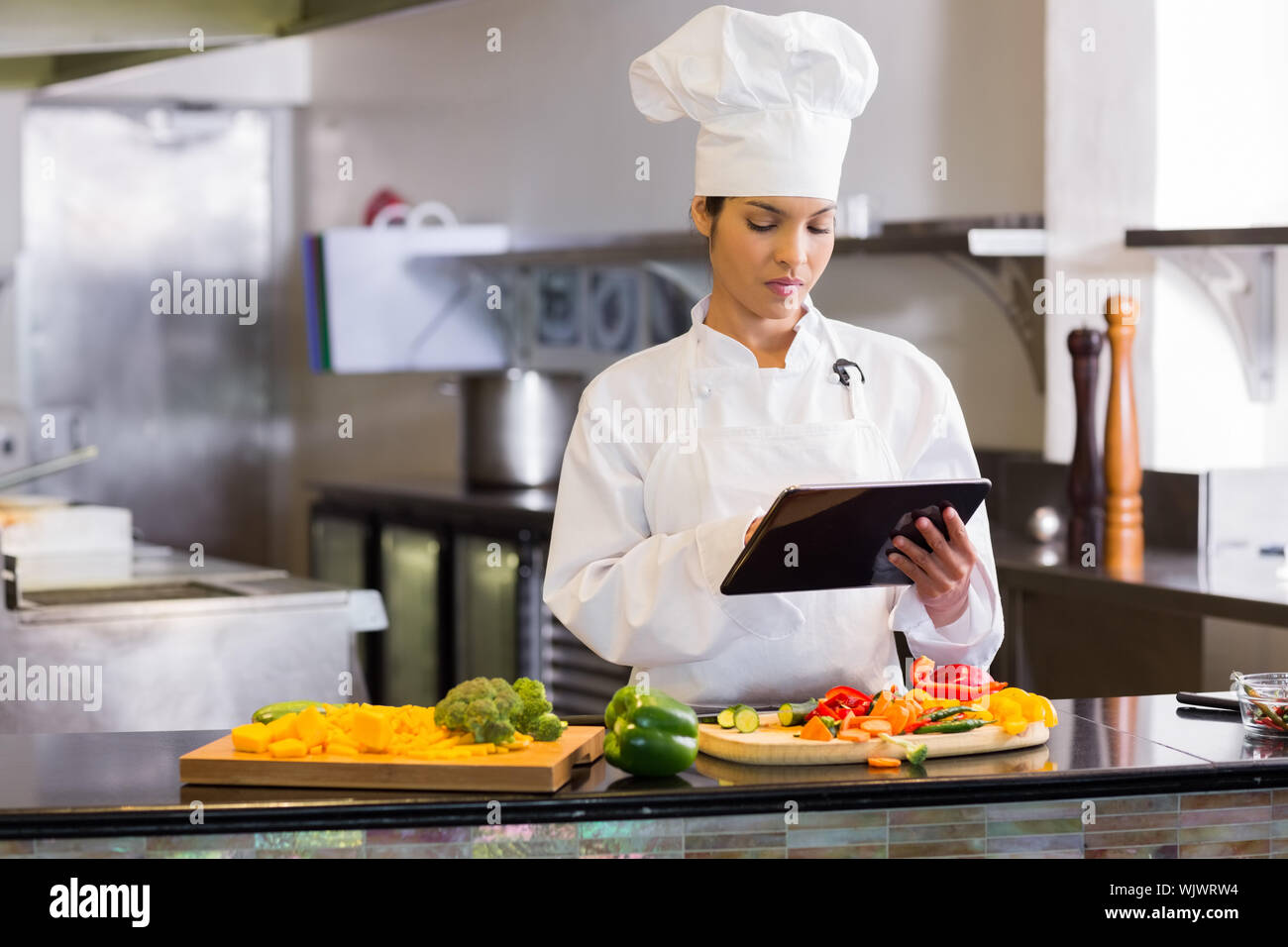 Concentrated young female chef using digital tablet while cutting ...