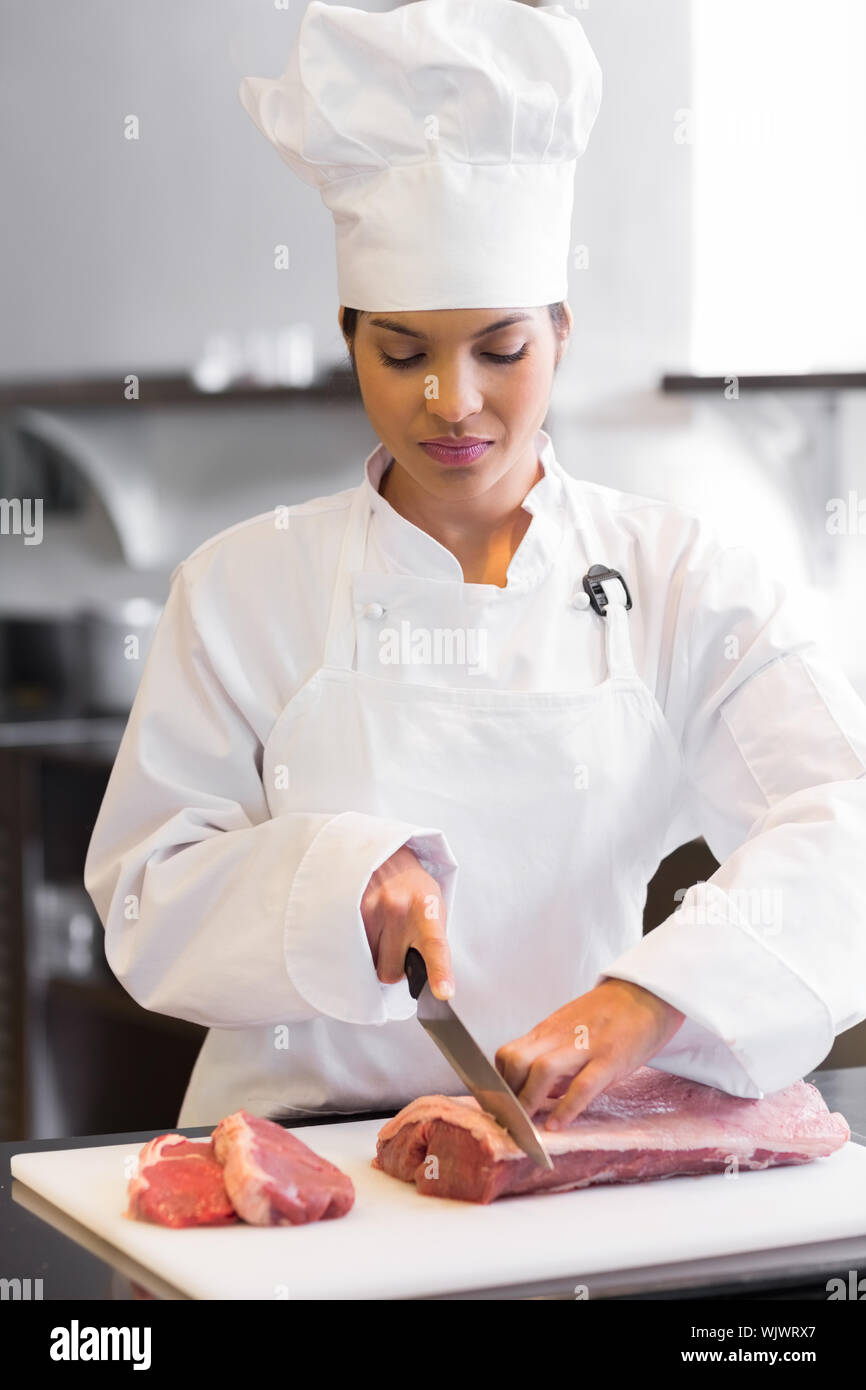 Concentrated young female chef cutting meat in the kitchen Stock Photo ...