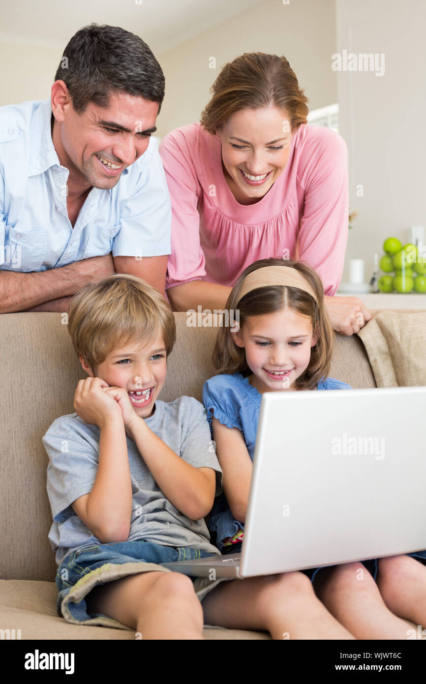 Happy parents watching children using laptop in living room Stock Photo ...