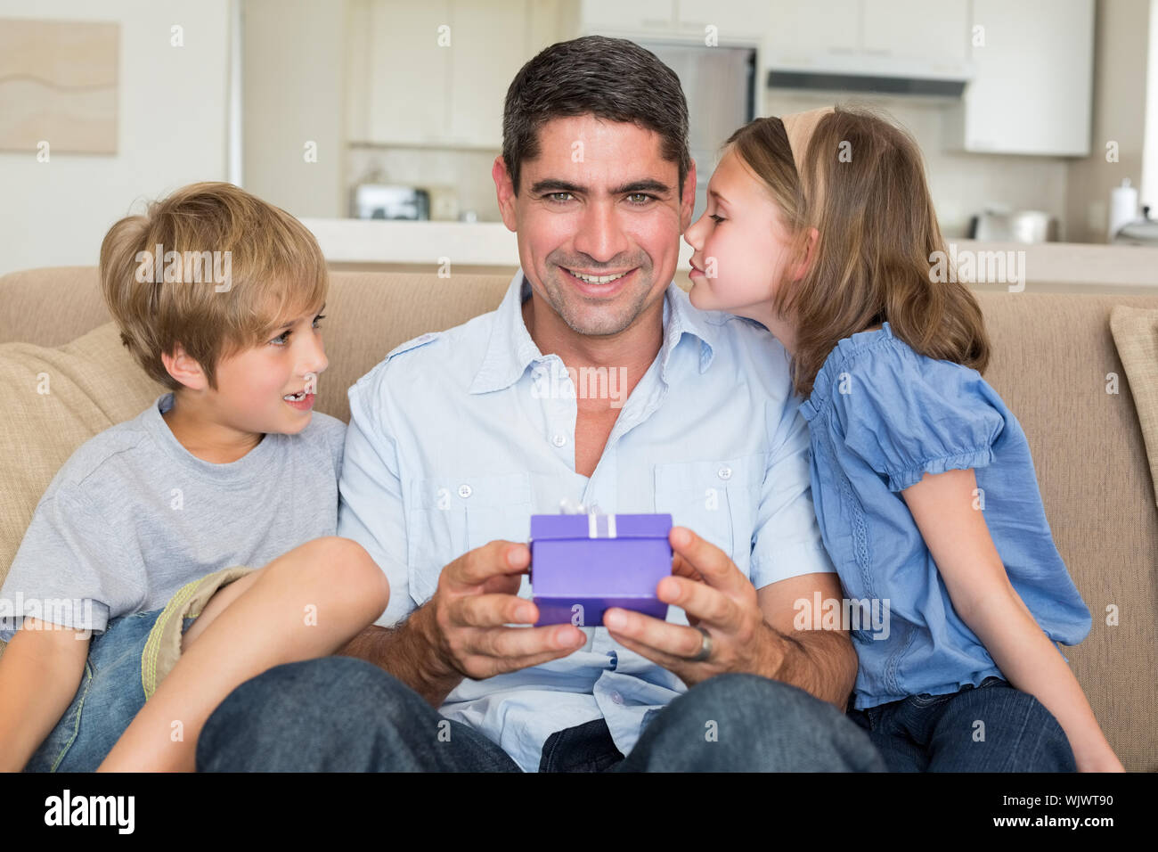 Portrait of father receiving gift from loving children in living room ...