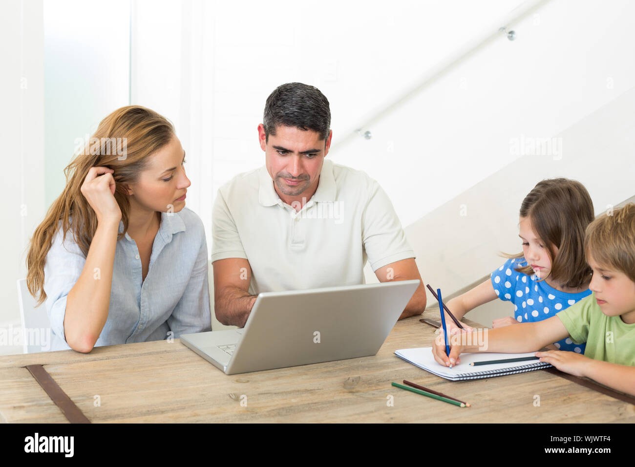 Parents using laptop while children coloring at table in house Stock ...