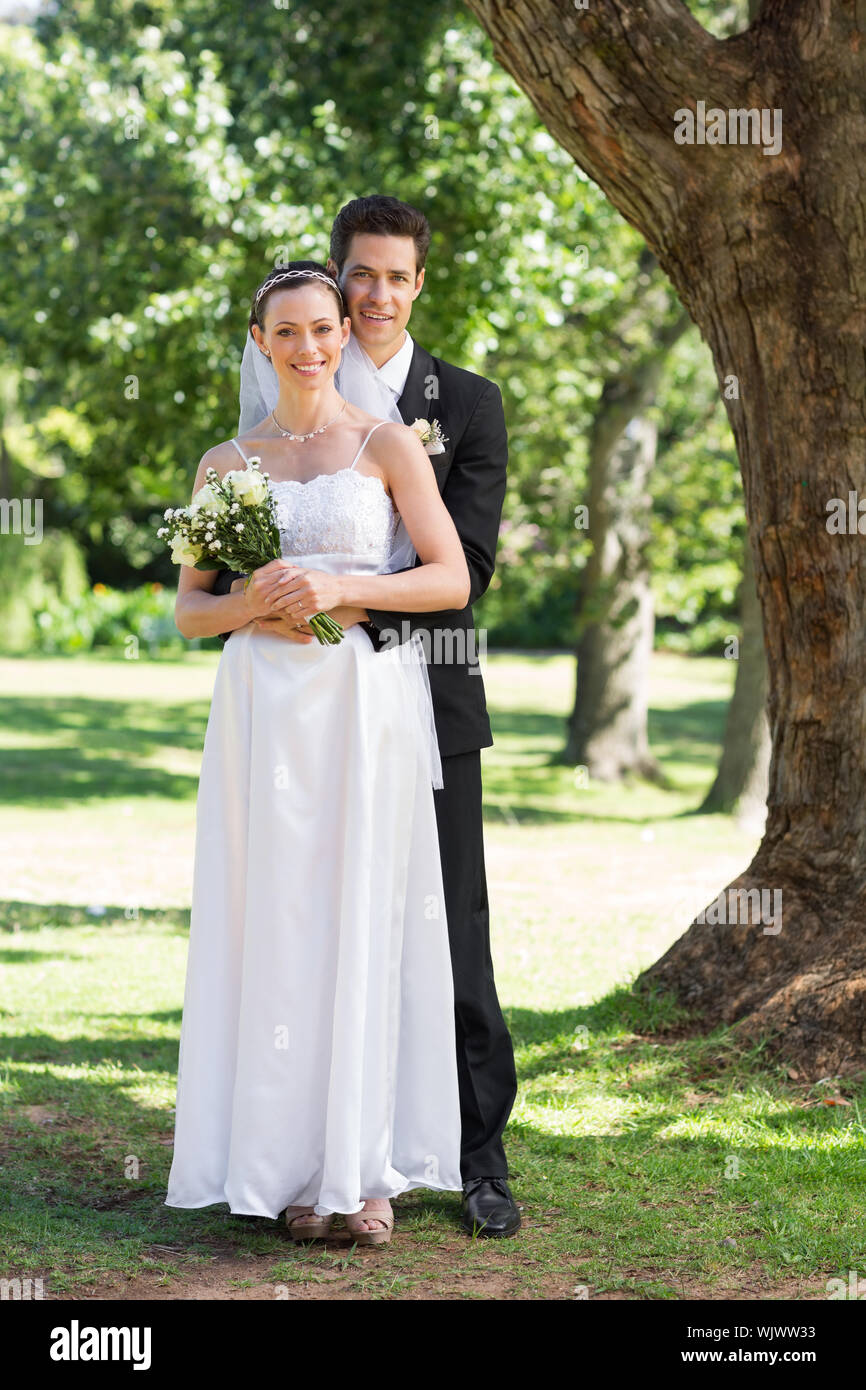 Full length portrait of groom and bride with flower bouquet in park ...