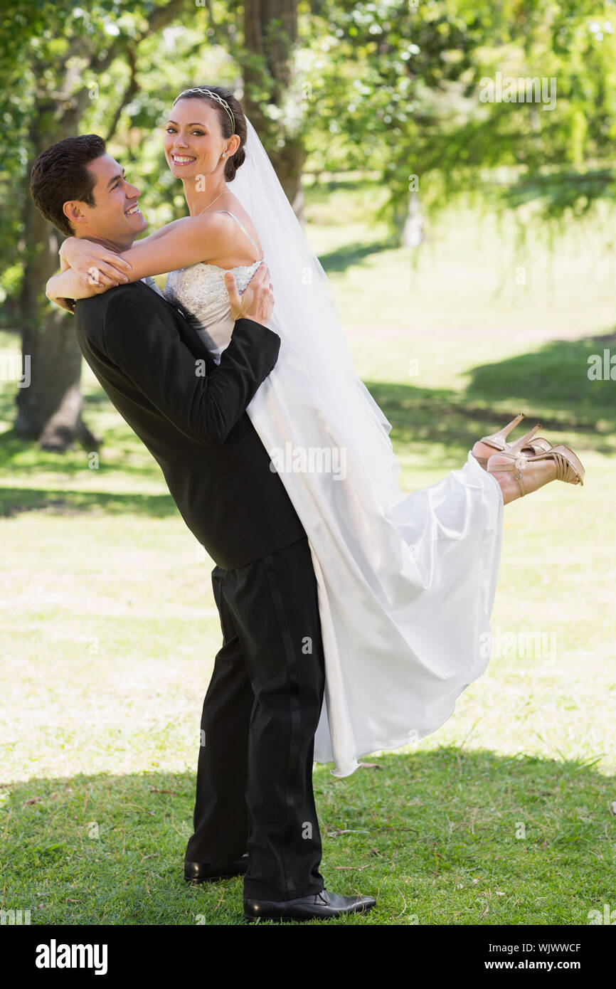 Full length side view of young groom lifting bride in garden Stock ...
