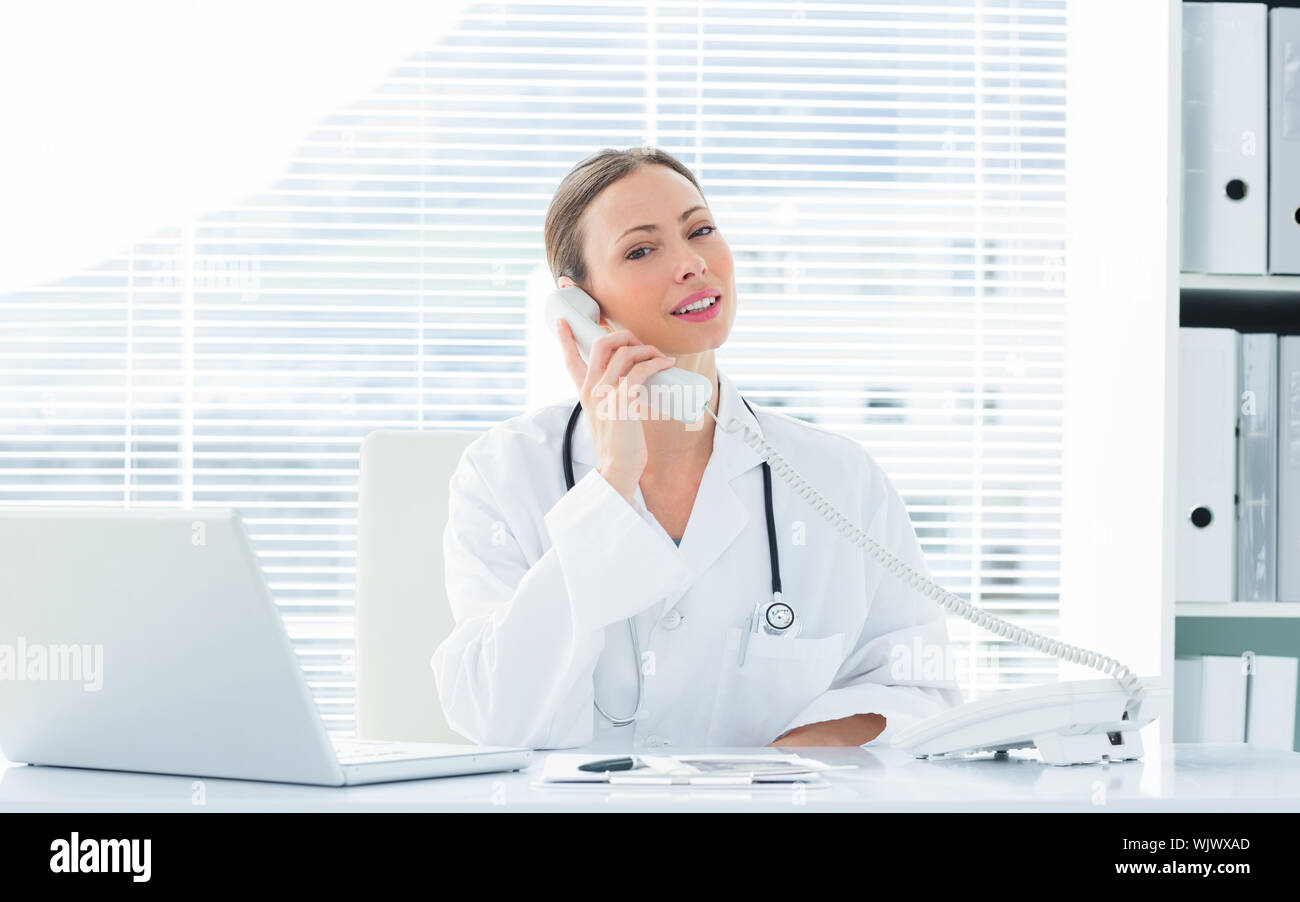 Portrait of confident female doctor using telephone at desk in clinic ...