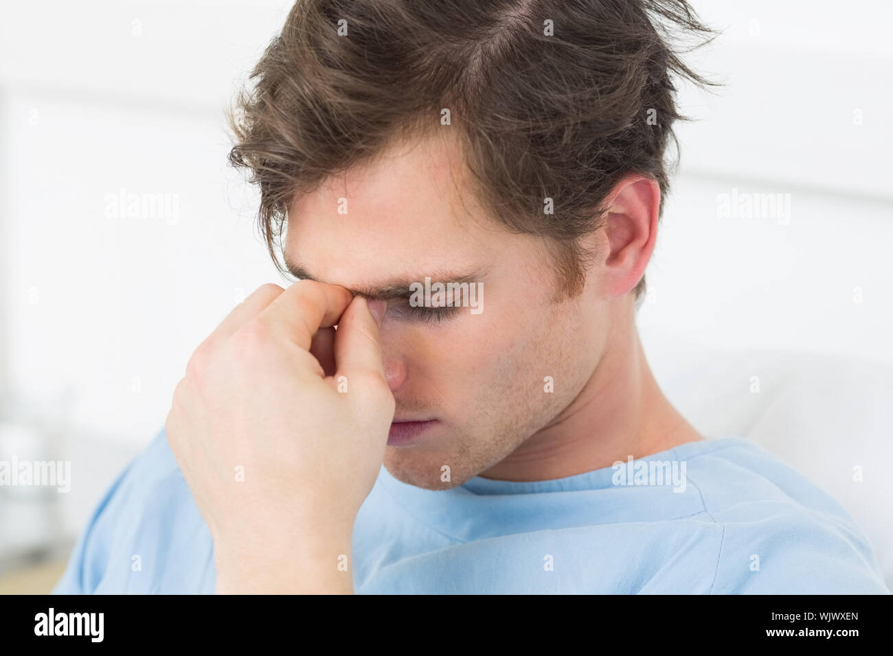 Tensed male patient suffering from headache relaxing on hospital bed ...