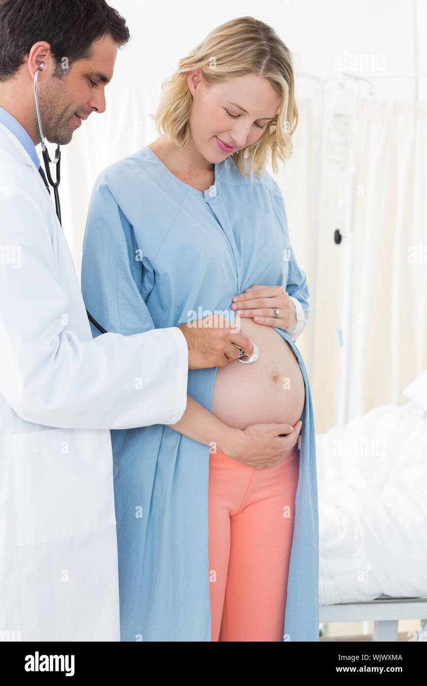 Male doctor checking belly of pregnant woman with stethoscope in ...