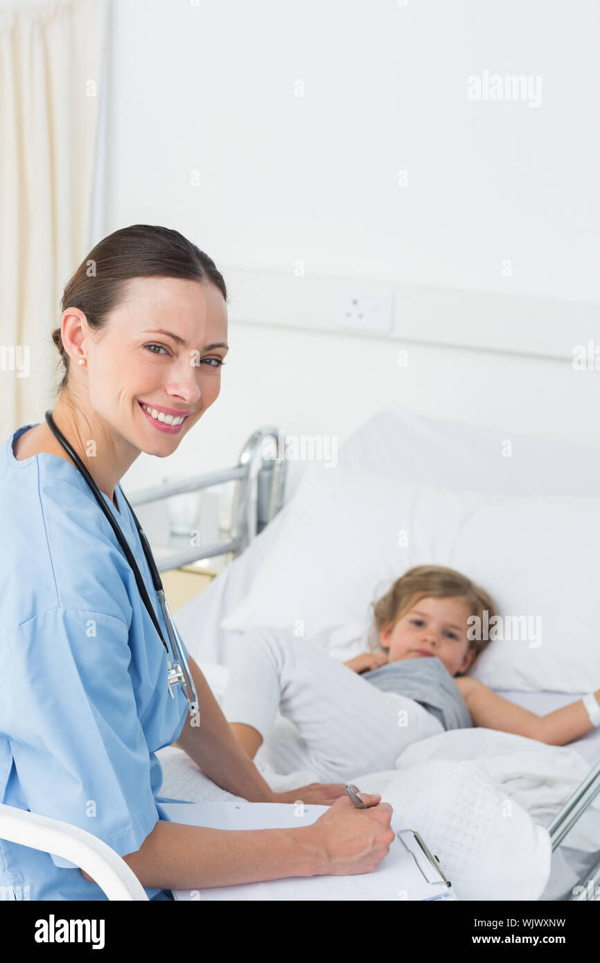 Portrait of smiling female doctor with clipboard attending sick girl in ...