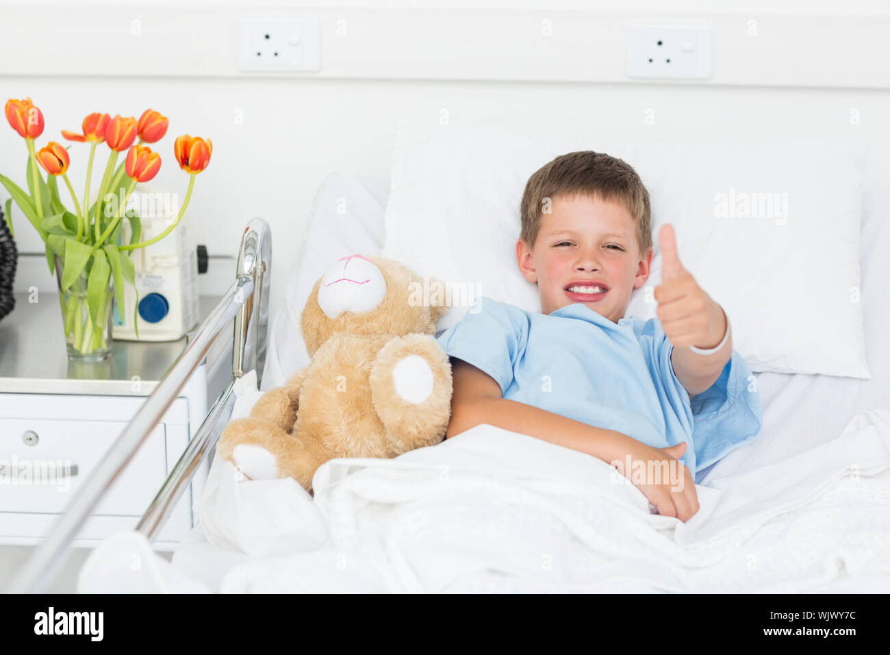 Portrait of little boy gesturing thumbs up with teddy bear in hospital ...