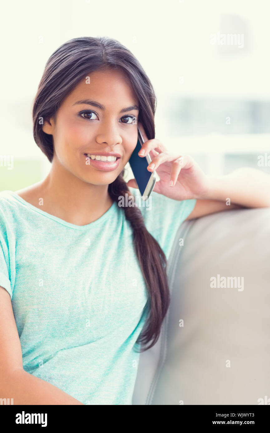 Happy girl sitting on sofa making a phone call at home in the living ...