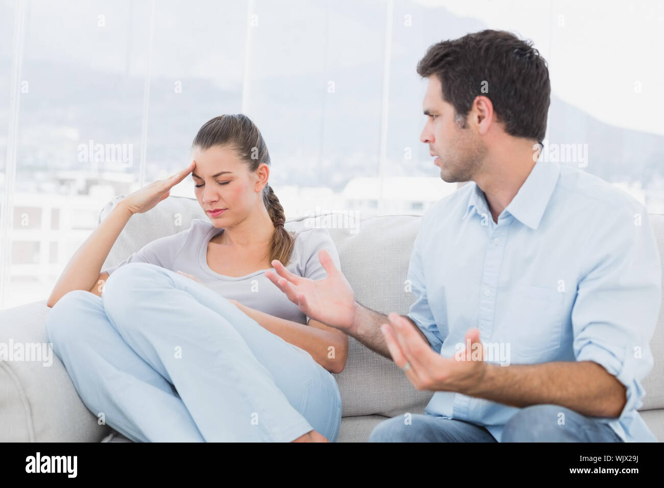 Man pleading with his upset partner on the couch at home in the living ...