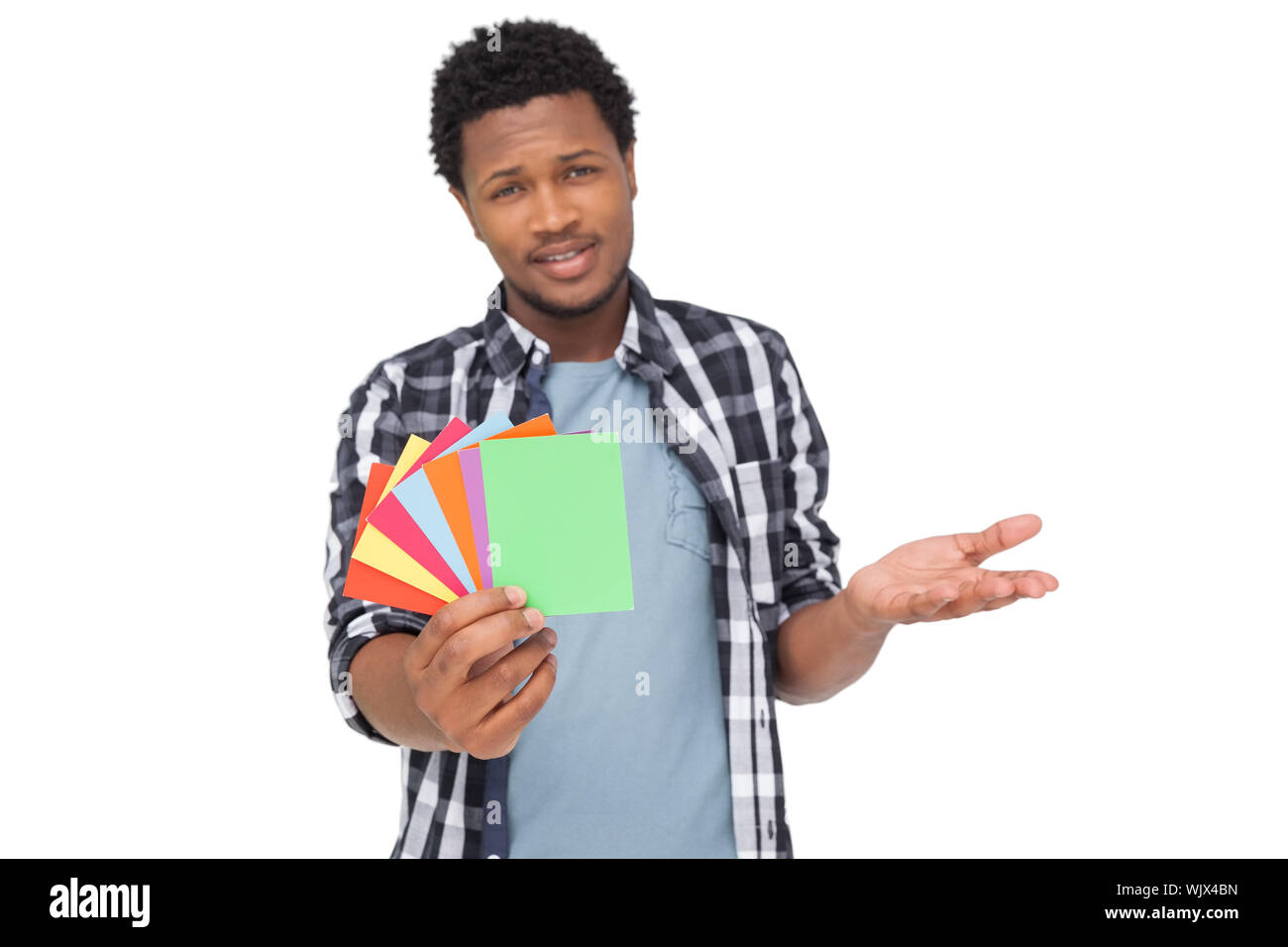 Portrait of a confused young man holding colorful papers over white ...