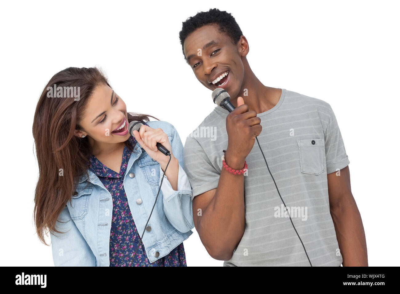 Portrait of a young couple singing into microphones over white ...