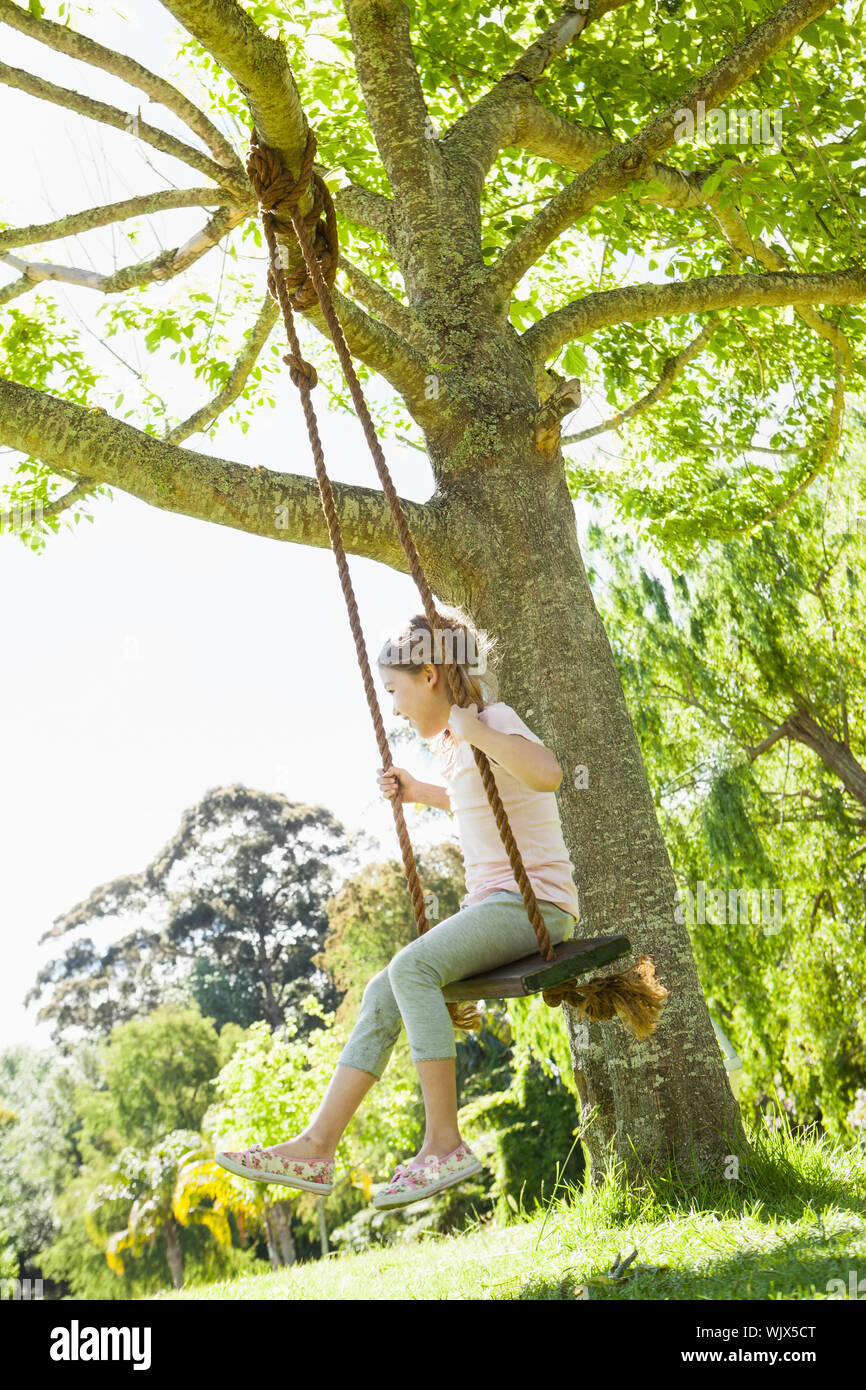 Full length side view of a young girl sitting on swing at the park ...
