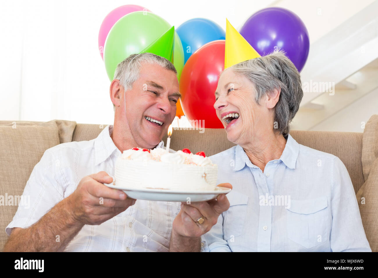 Senior couple sitting on couch celebrating a birthday at home in living ...