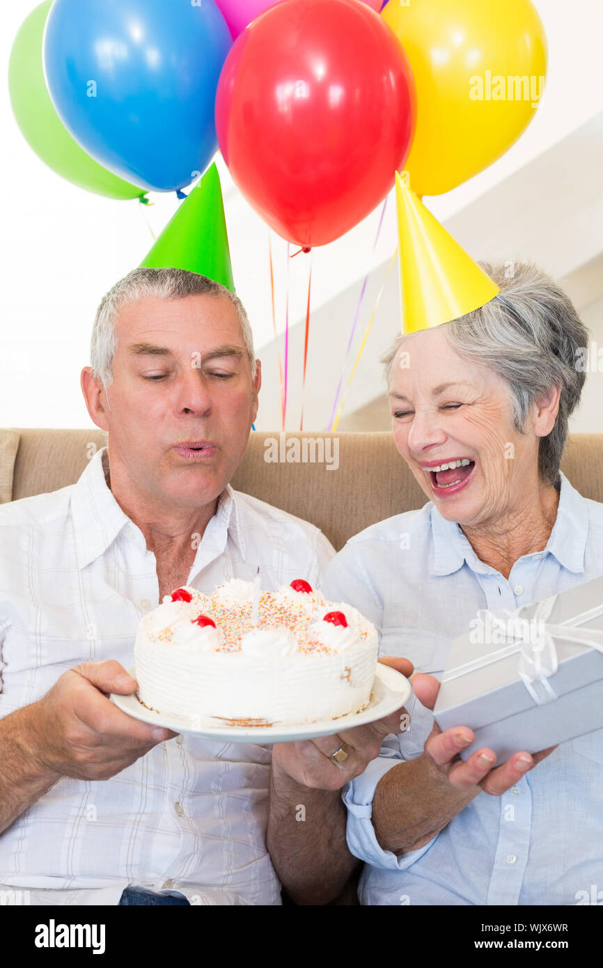 Senior couple sitting on couch celebrating a birthday at home in living ...