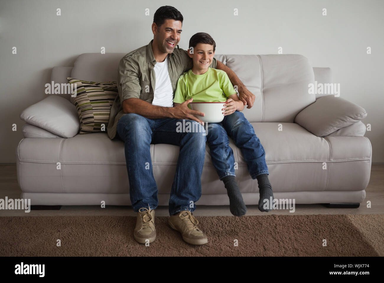 Full length of a happy father and son with popcorn bowl watching tv in ...
