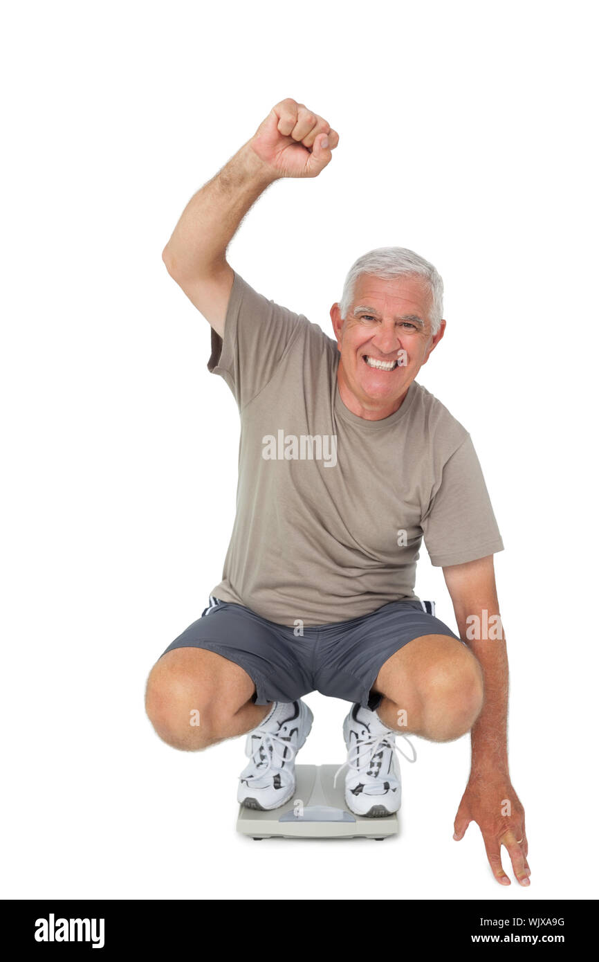 Full length portrait of a senior man cheering on weight scale over ...