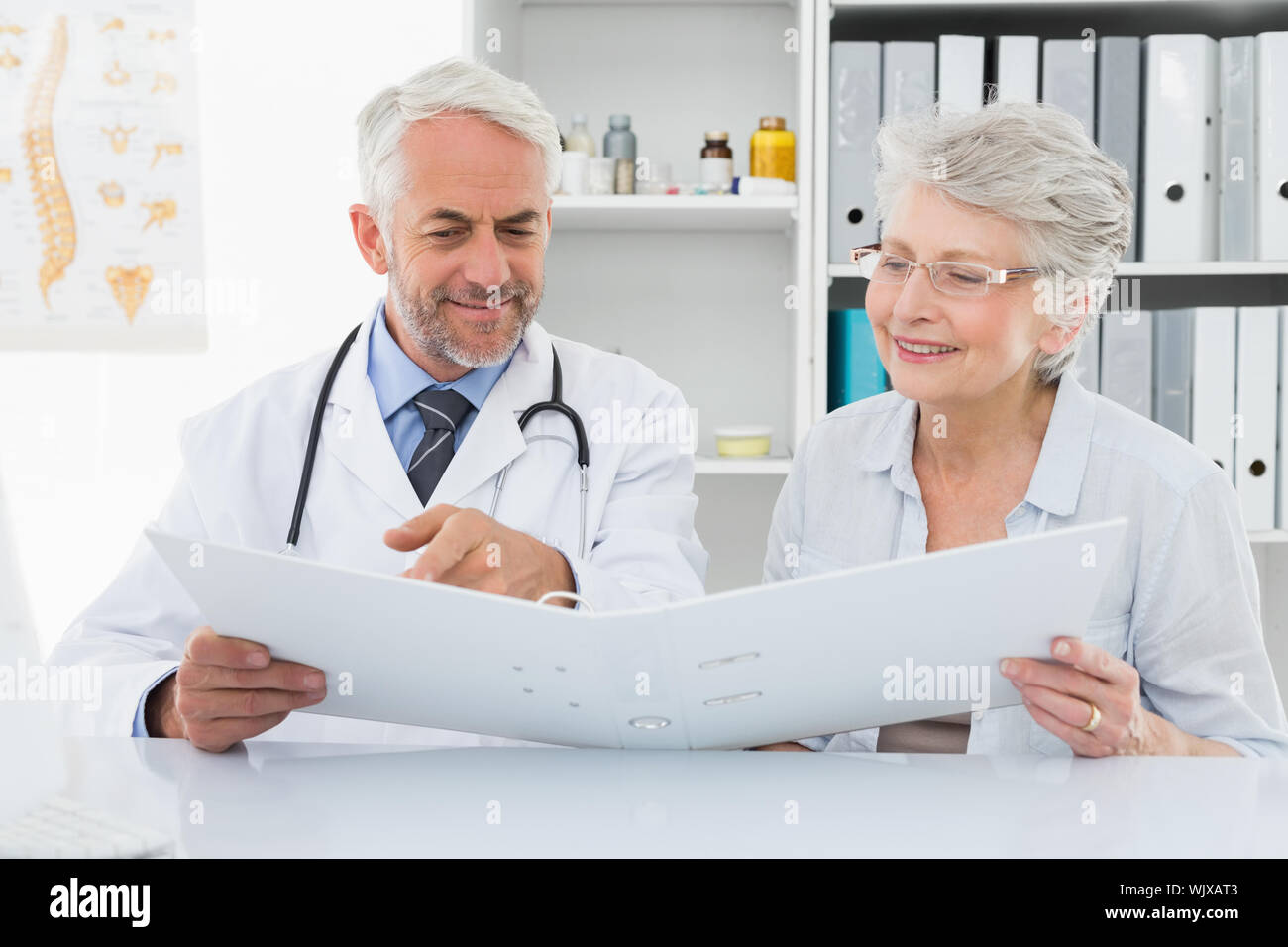 Male doctor with female patient reading reports at medical office Stock ...