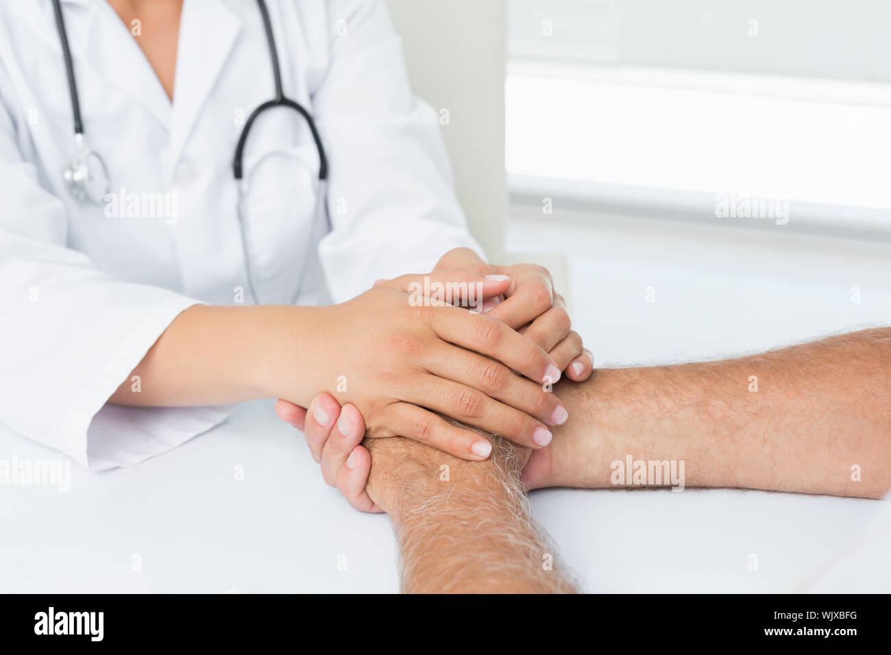 Close-up mid section of a doctor holding patients hands at medical ...