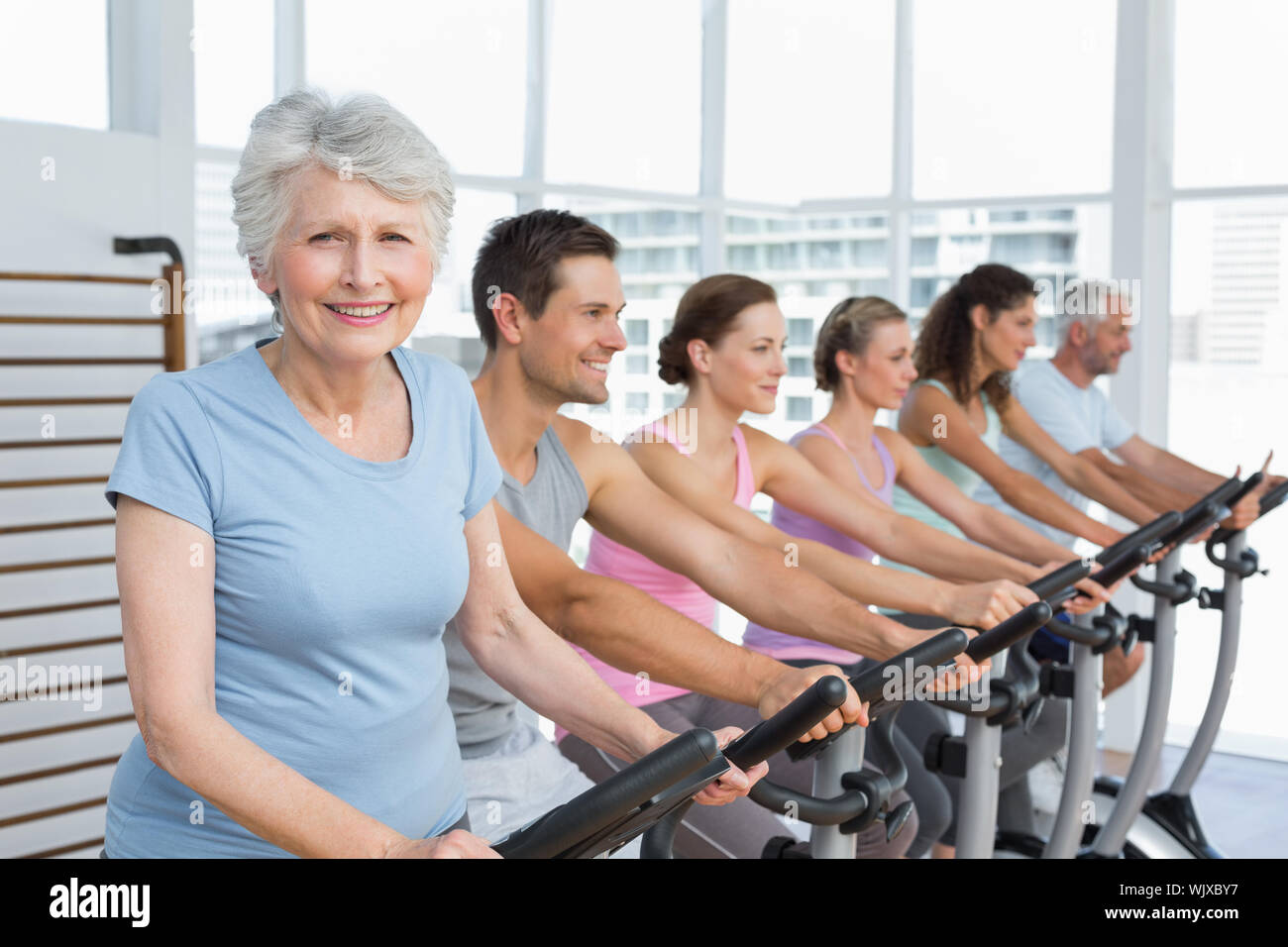 Group portrait of happy people working out at spinning class in gym ...