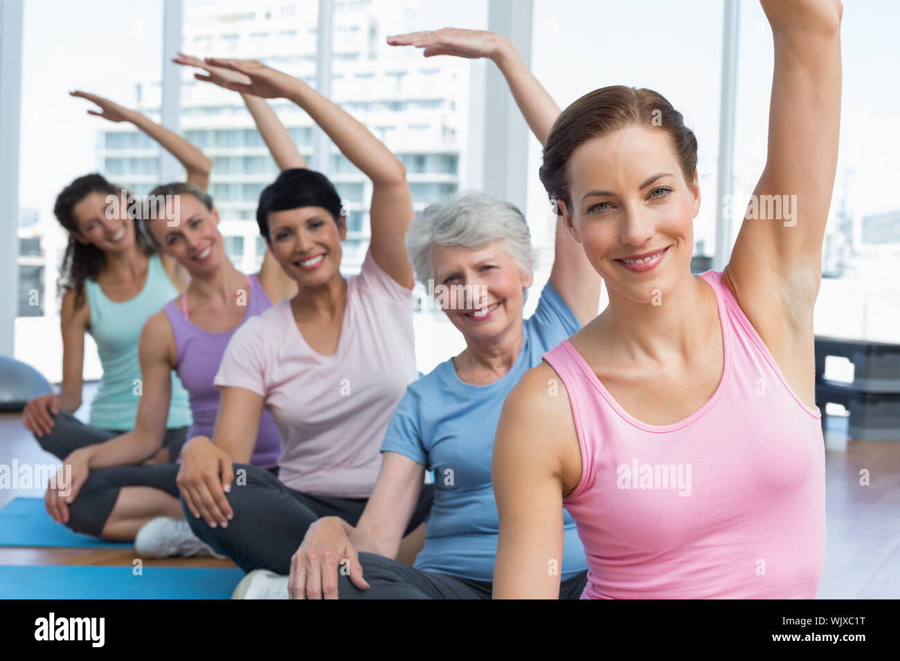 Portrait of a smiling trainer with women in row stretching hands at ...