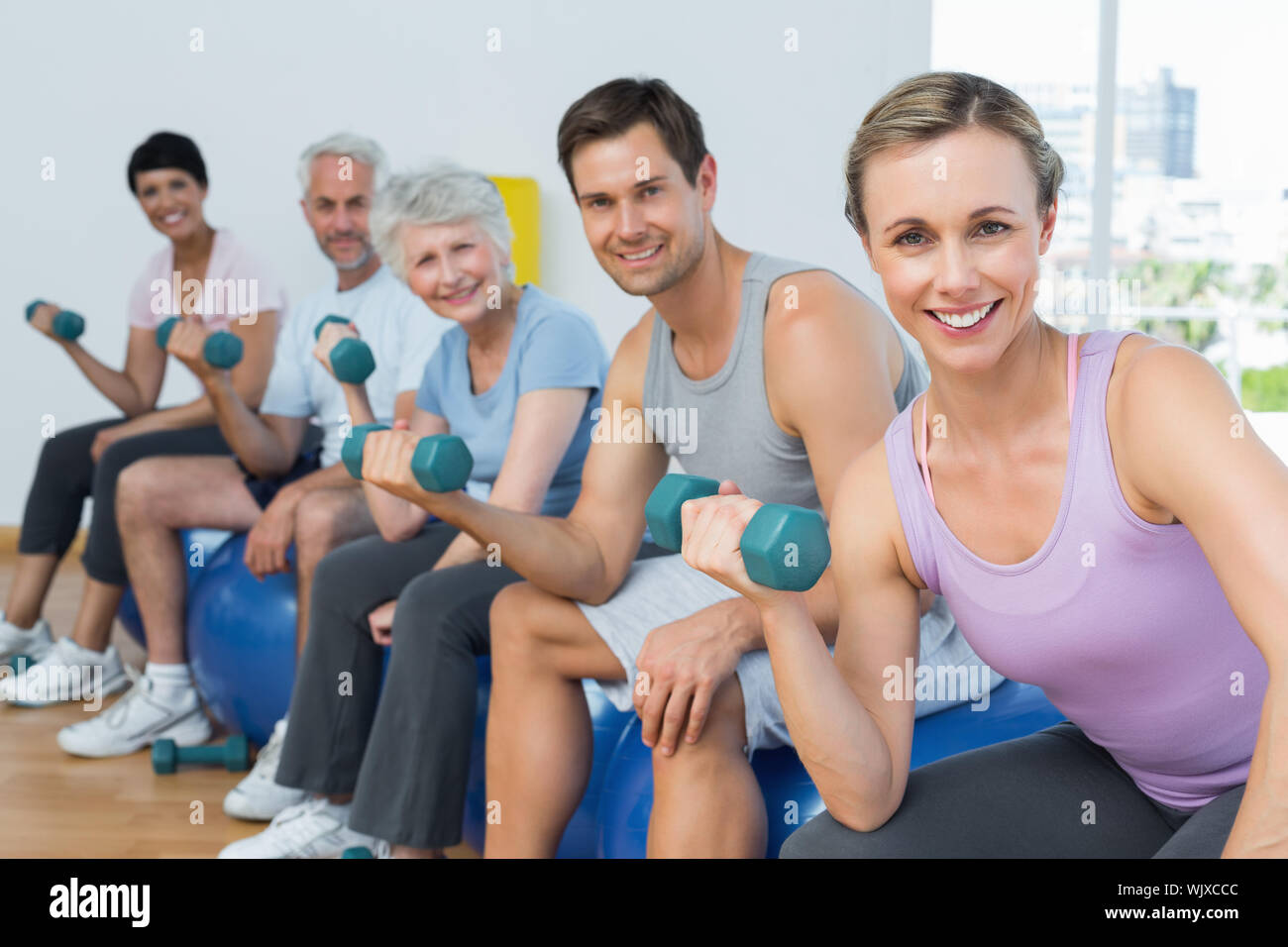 Side view of fitness class exercising with dumbbells in a bright gym ...