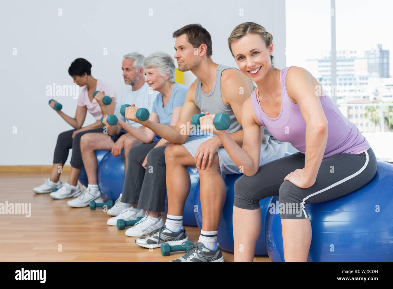 Side view of fitness class with dumbbells sitting on exercise balls in ...