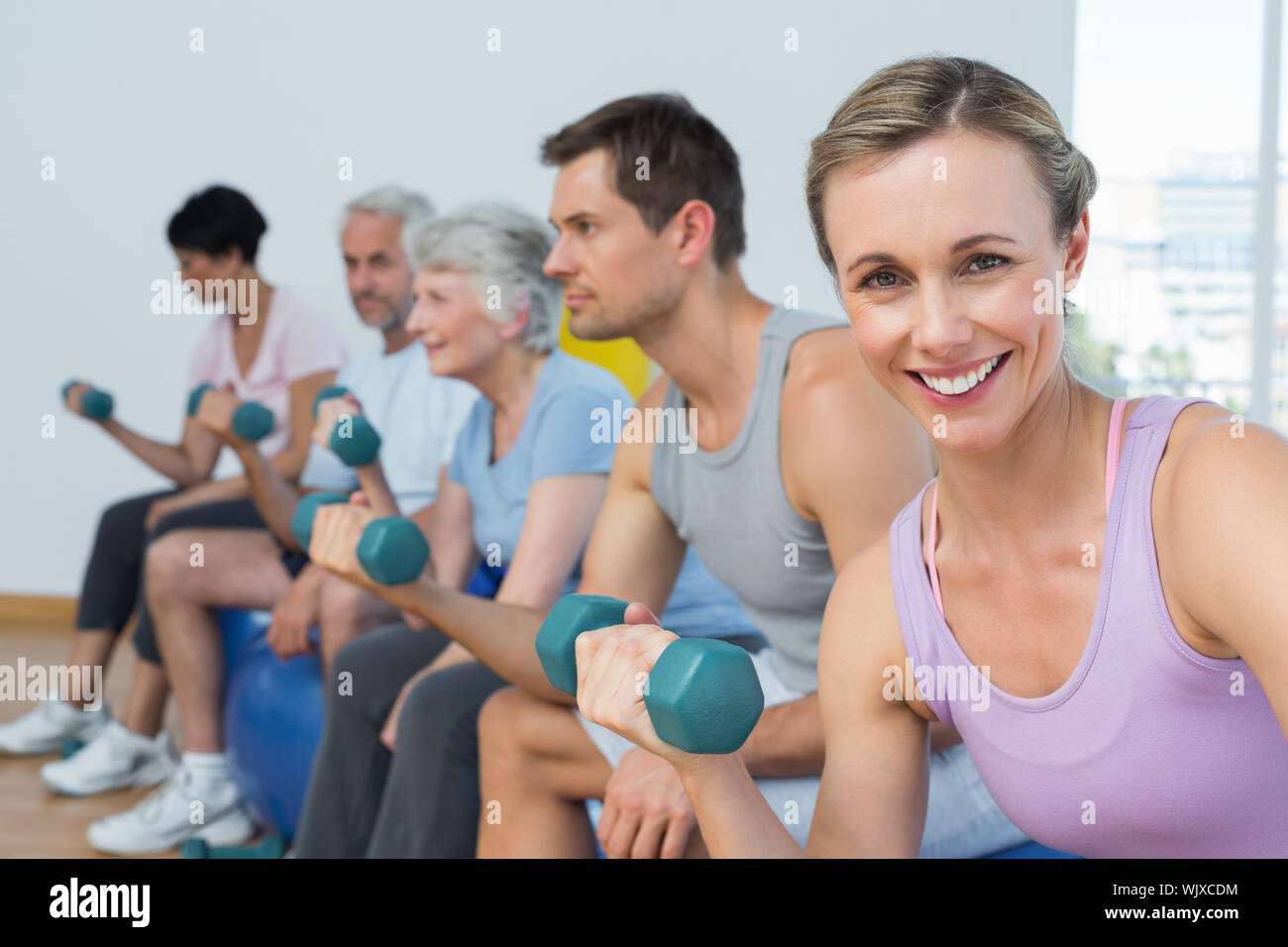 Side view of fitness class with dumbbells sitting on exercise balls in ...