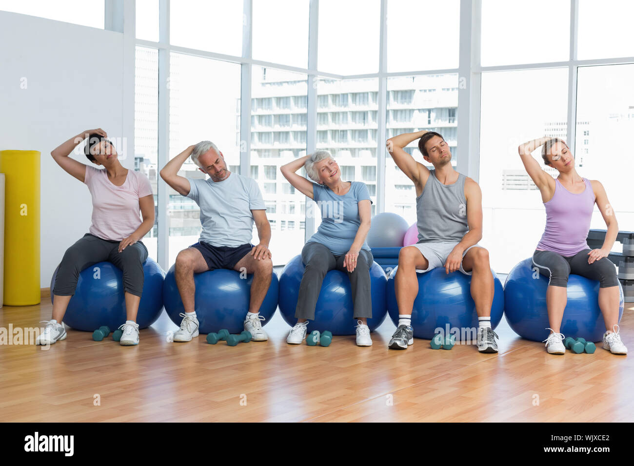 Fitness class sitting on exercise balls and stretching neck in a bright ...