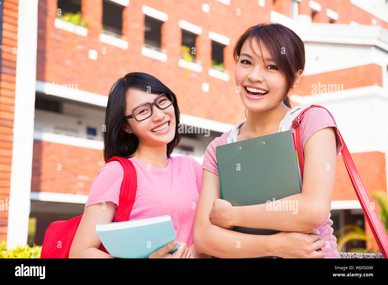 two smiling students holding books at campus Stock Photo - Alamy