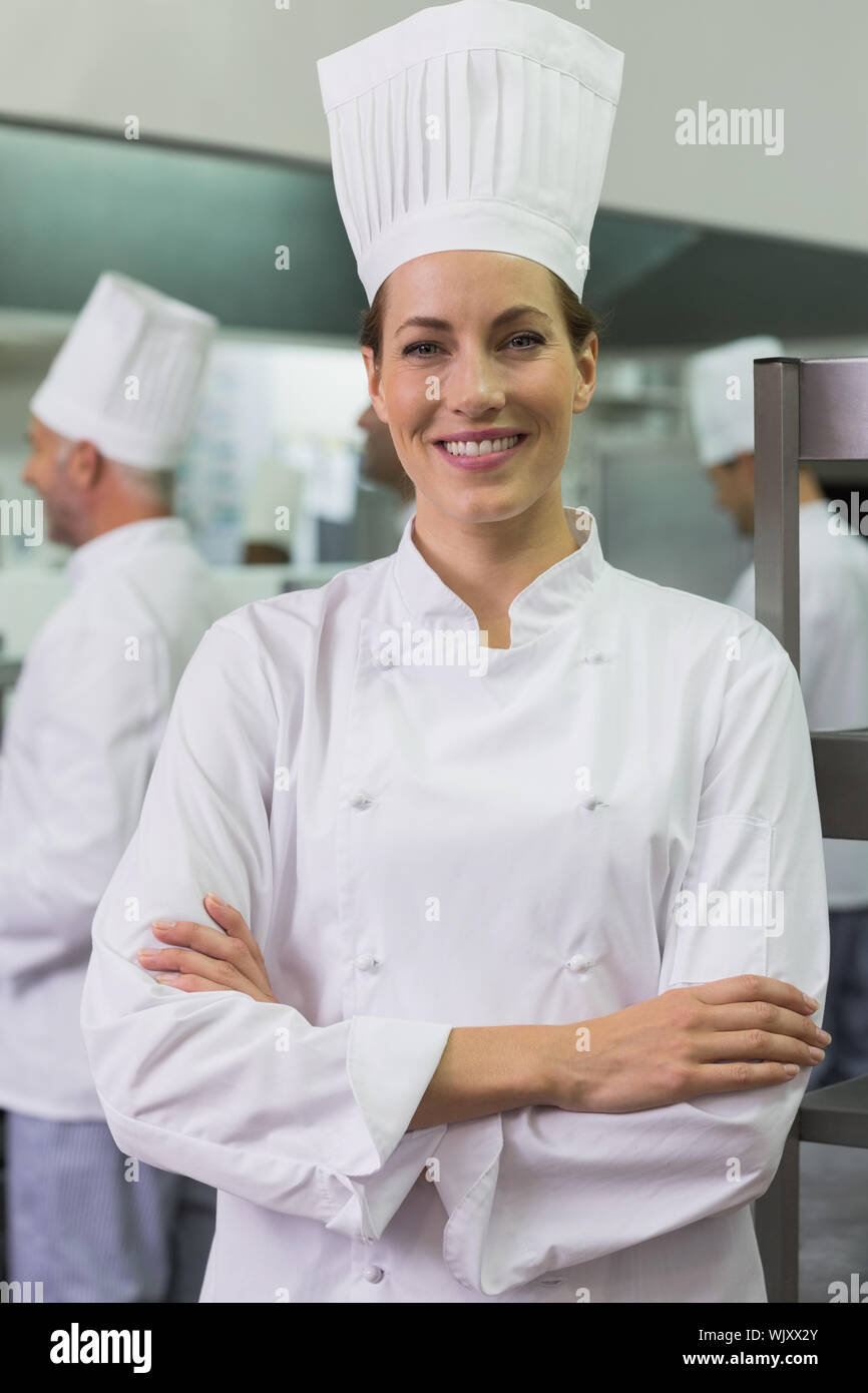 Smiling chef looking at camera with team working behind in a commercial ...