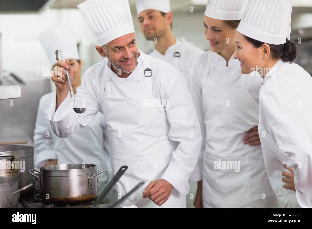 Head chef tasting a soup while staff watch in a commercial kitchen ...
