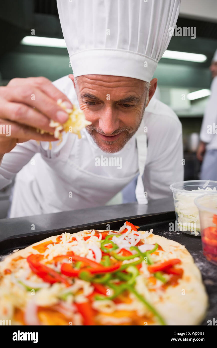 Happy chef sprinkling cheese on a pizza in a commercial kitchen Stock ...