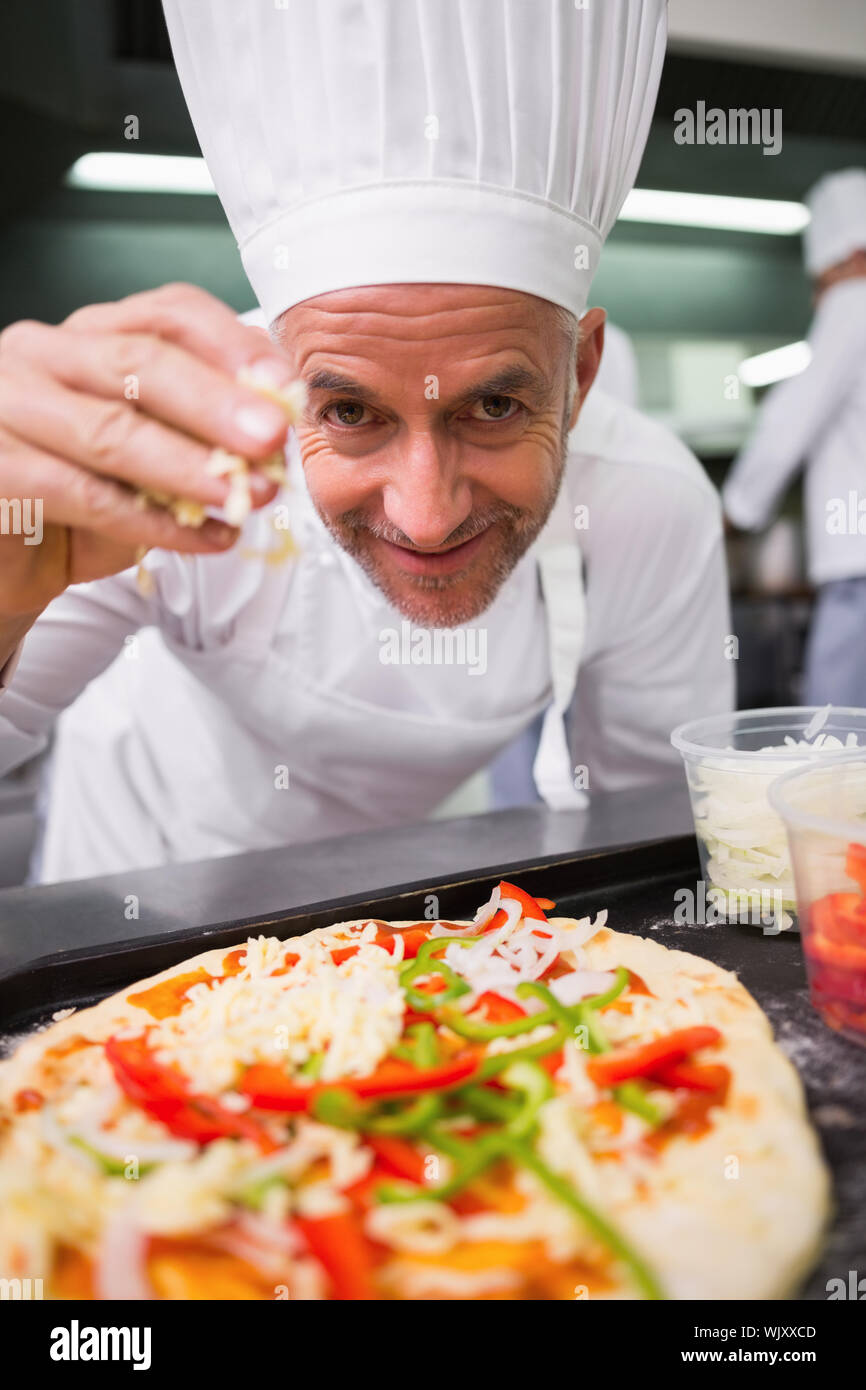 Happy chef sprinkling cheese on a pizza in a commercial kitchen Stock ...