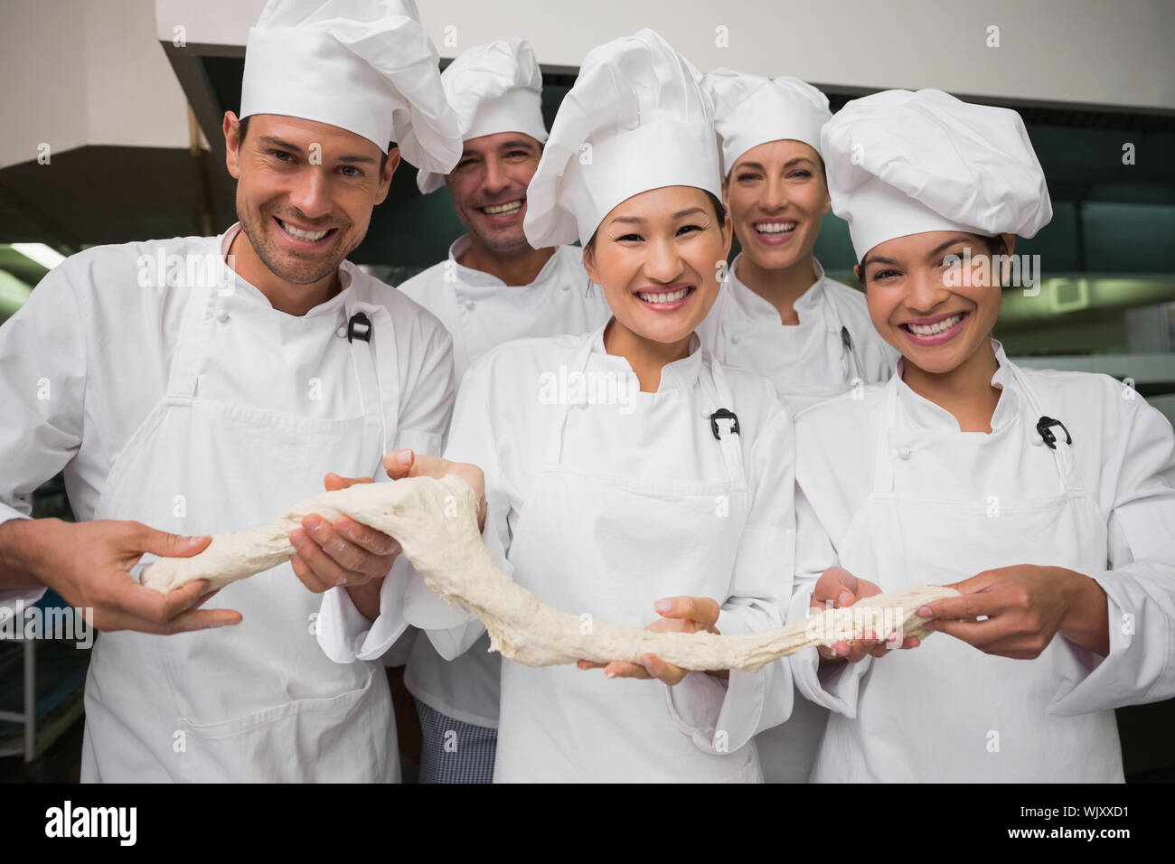 Chefs holding a stretched piece of dough smiling at camera in a ...