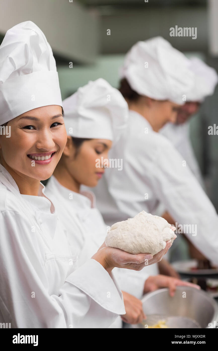 Happy chef holding dough smiling at camera in a commercial kitchen ...