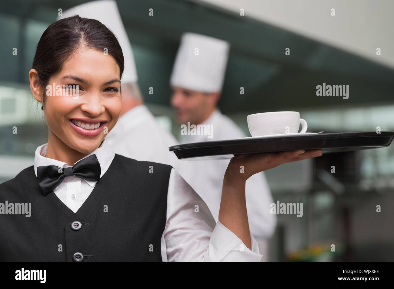 Happy waitress holding tray with coffee cup in a commercial kitchen ...