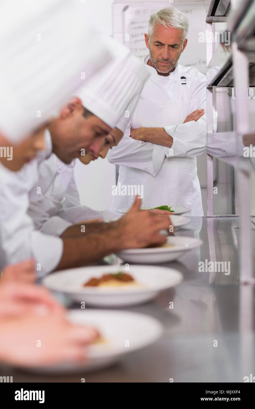 Head chef watching row of chefs garnishing spaghetti dishes with basil ...