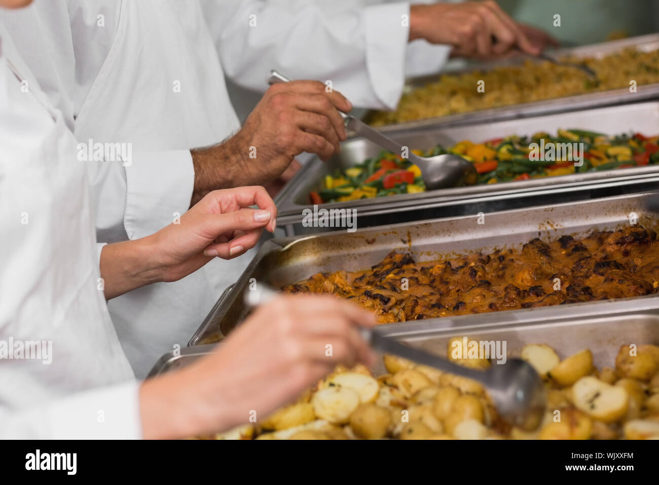 Chefs serving hot food from serving trays in a commercial kitchen Stock ...
