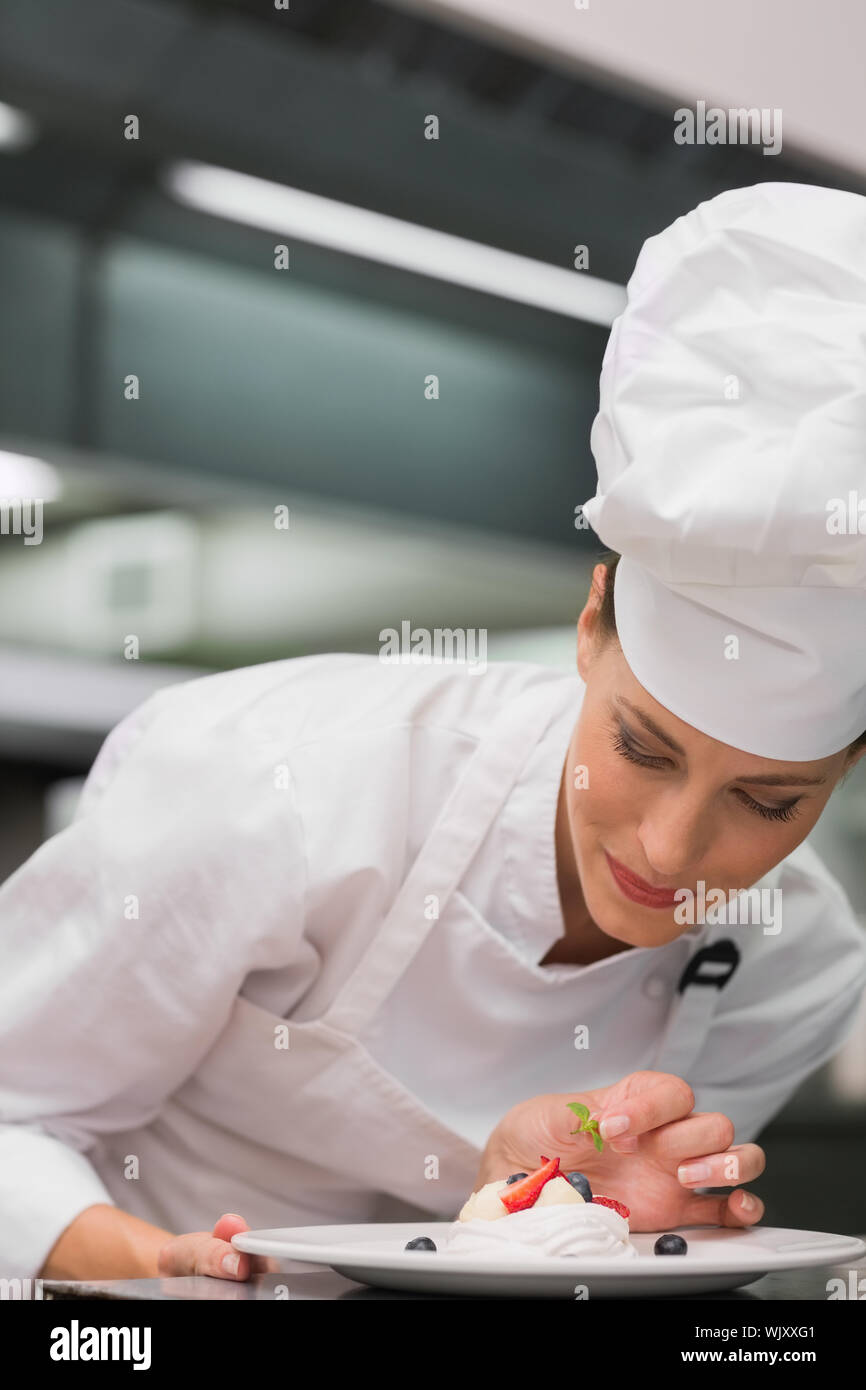 Smiling chef putting mint leaf on meringue dish in a commercial kitchen ...