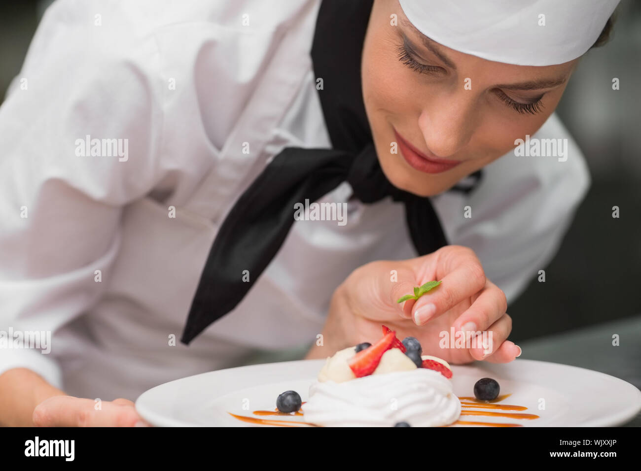 Smiling chef putting mint leaf on meringue dish in a commercial kitchen ...