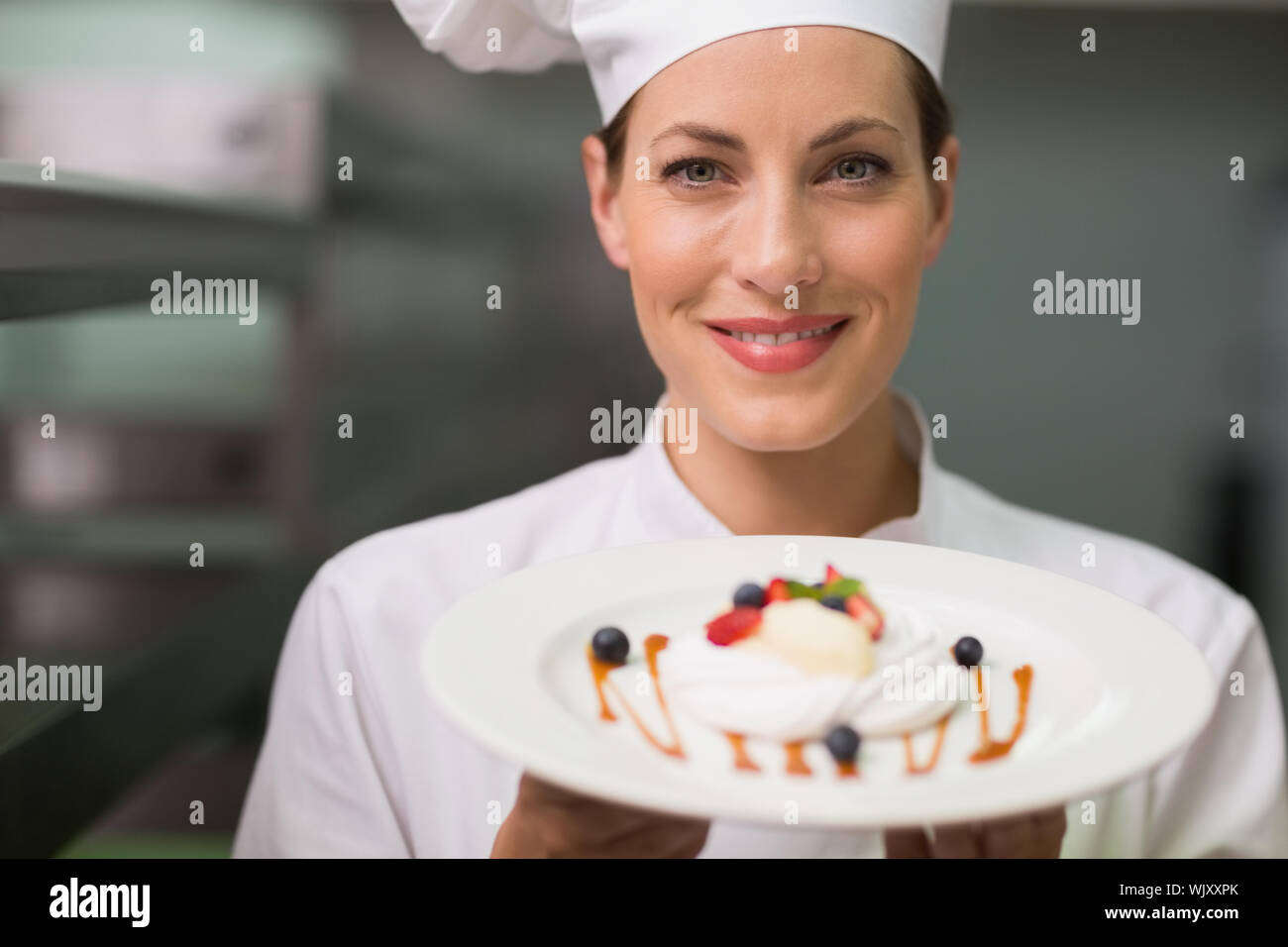 Happy chef smiling at camera holding dessert plate in a commercial ...