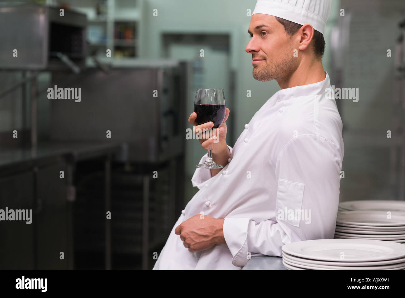 Chef relaxing with glass of red wine after work in a commercial kitchen ...