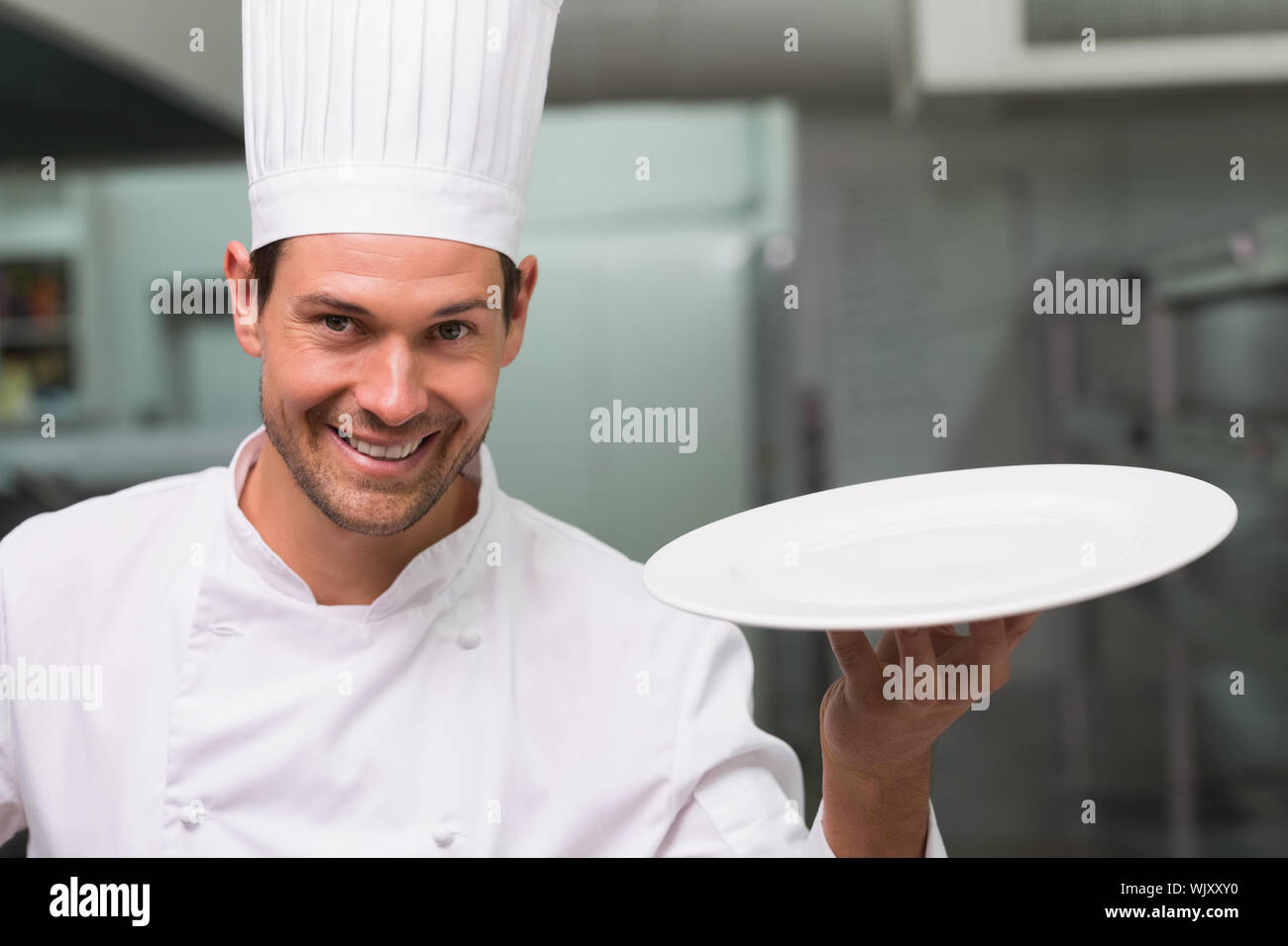 Chef holding a plate smiling at camera in a commercial kitchen Stock ...