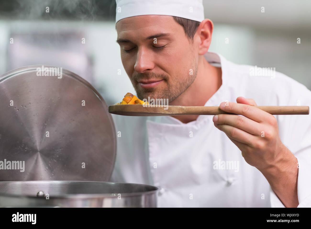 Chef smelling a spoon of food from the pot in a commercial kitchen ...