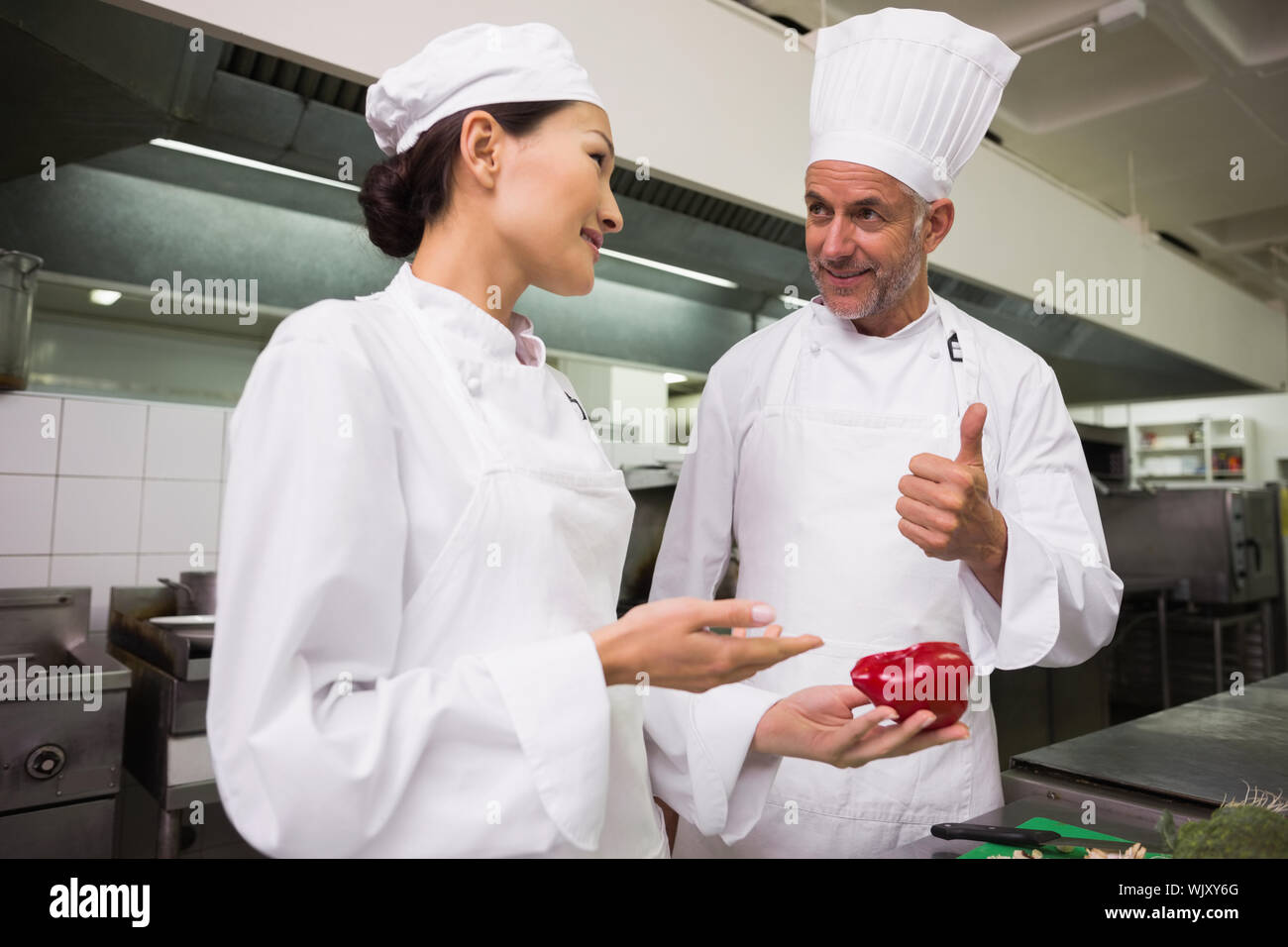 Chef teaching trainee how to slice vegetables in a commercial kitchen ...