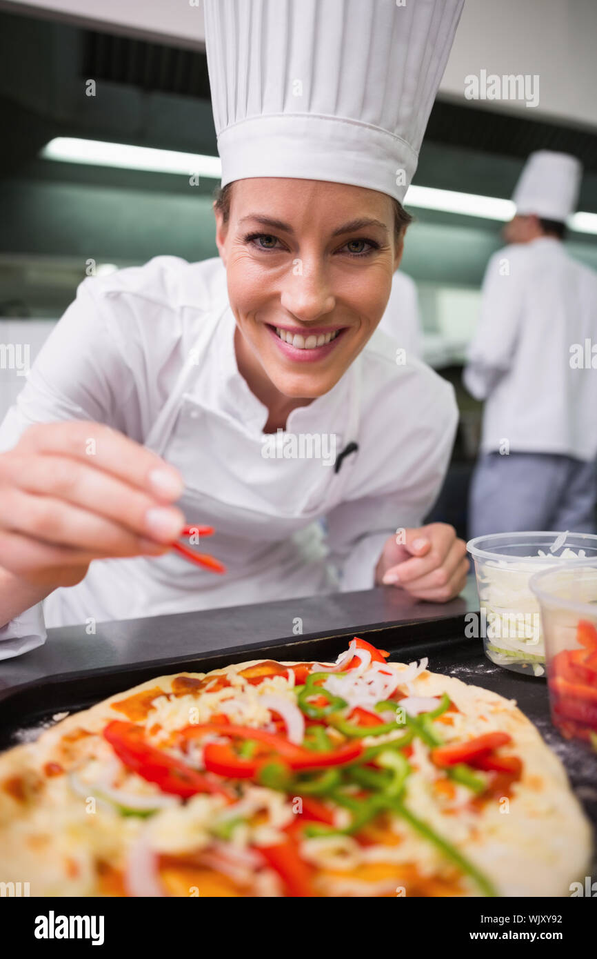 Happy chef sprinkling pepper on a pizza in a commercial kitchen Stock ...