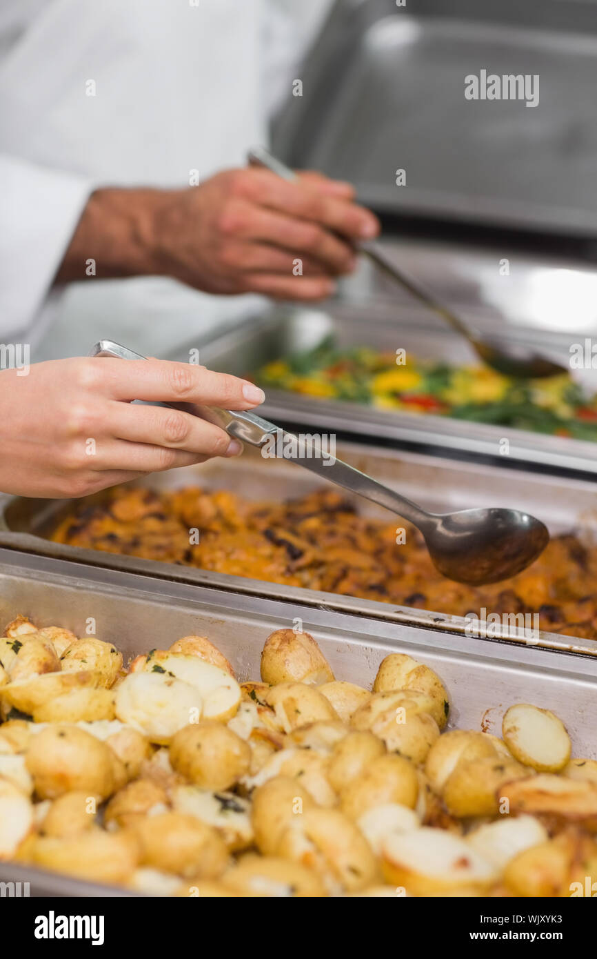 Chefs dishing up food from serving trays in a commercial kitchen Stock ...